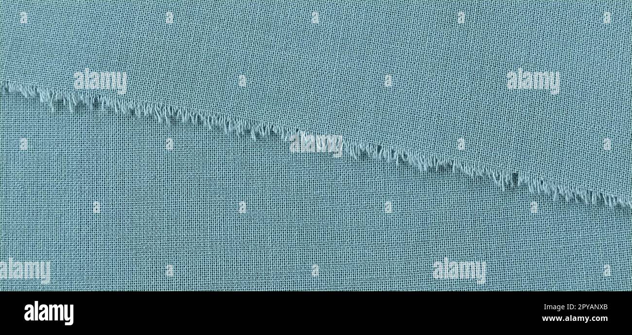 Ripped edge of fine woolen fabric in green or blue. Loose threads at ...