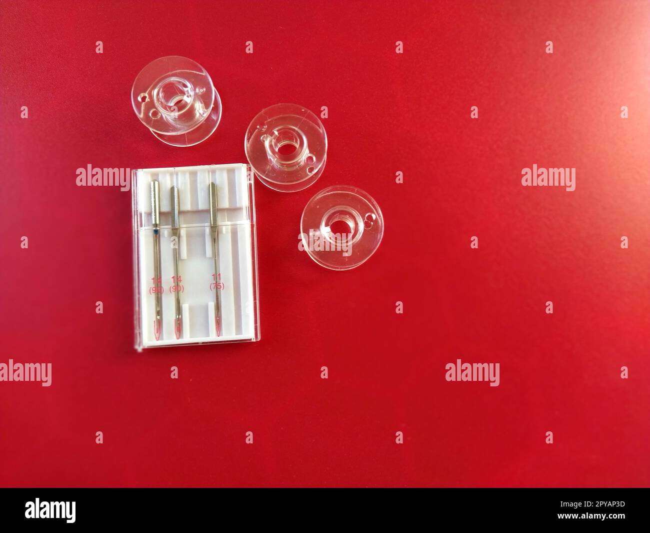 plastic bobbins and a set of sewing machine needles on a red background ...