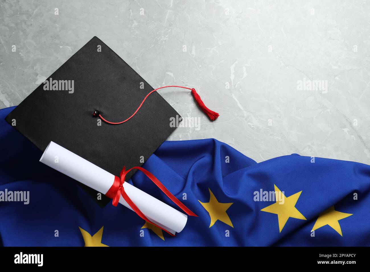Black graduation cap, diploma and flag of European Union on light grey ...