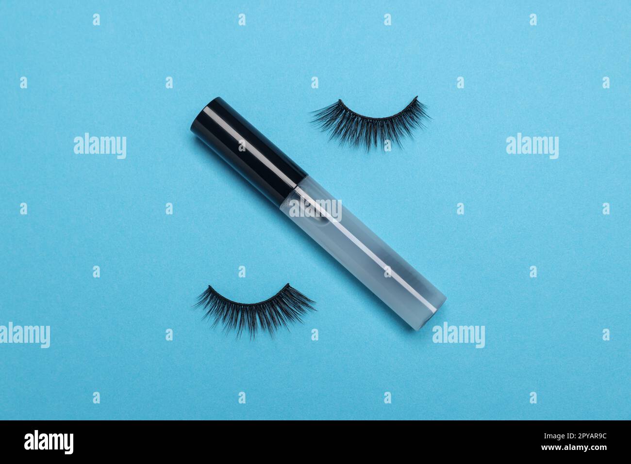 False eyelashes and tube of oil on light blue background, flat lay ...