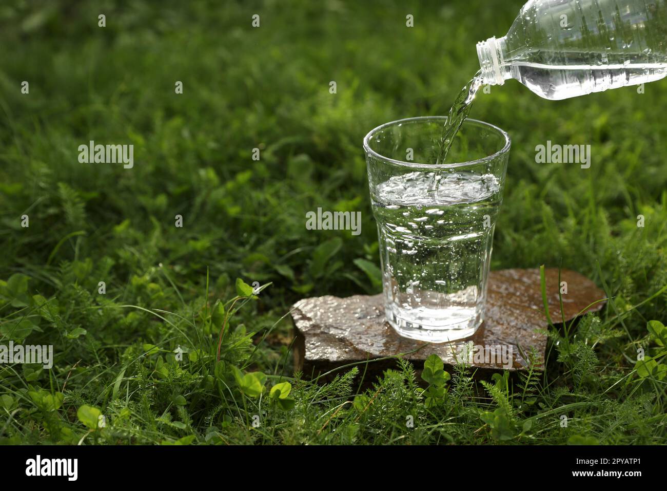 Pouring fresh water from bottle into glass on stone outdoors. Space for ...