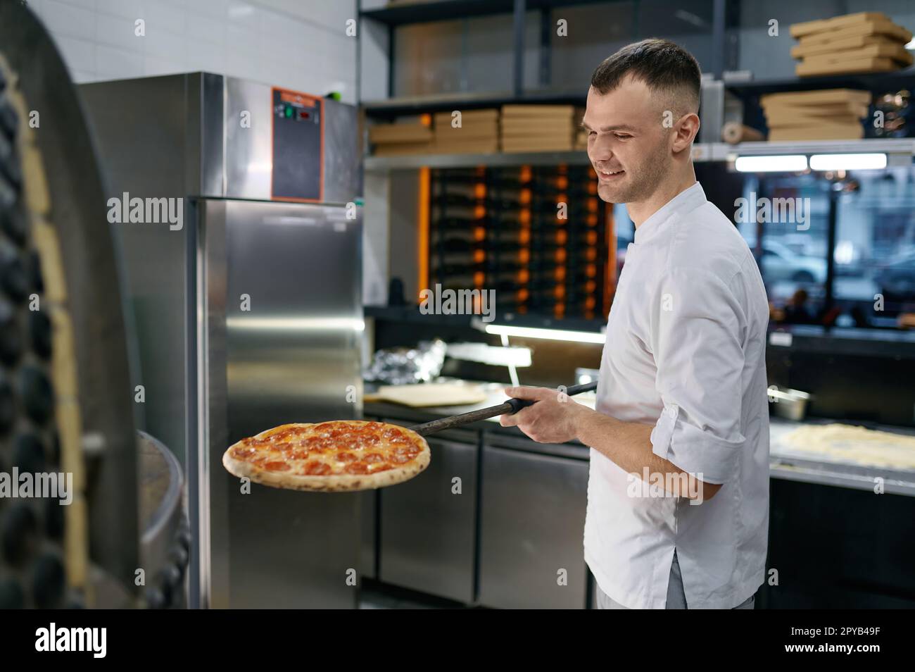 Cheerful young man working in pizza shop presenting fresh baked pastry ...