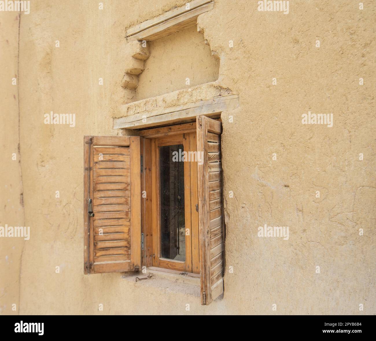 Old rustic wooden window with shutters in wall of traditional mud brick ...