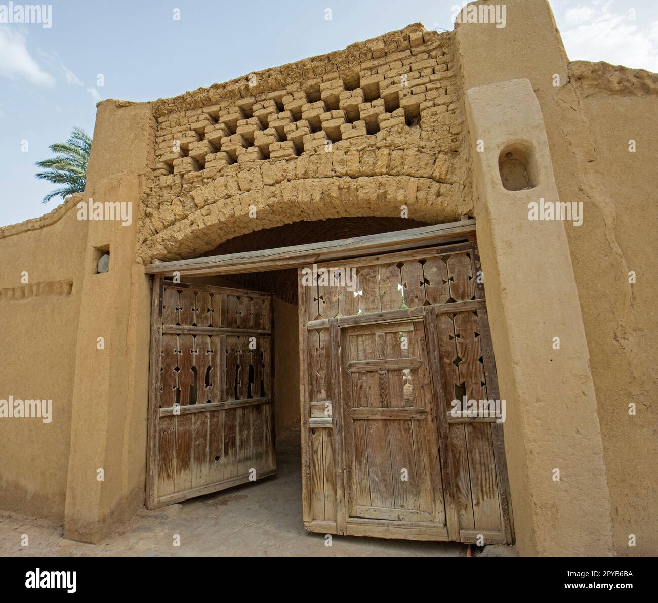 Old rustic wooden door entrance gate in wall of traditional mud brick ...