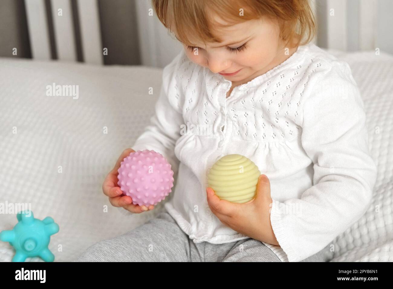 Cute baby girl playing tactile knobby balls. Young child hand plays ...