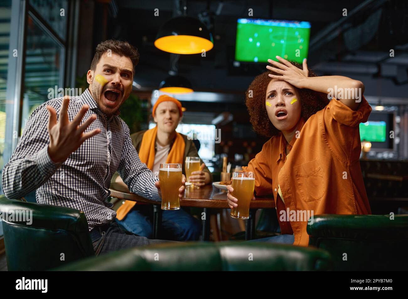 Cheering friends of soccer fans with creative makeup in faces in pub ...