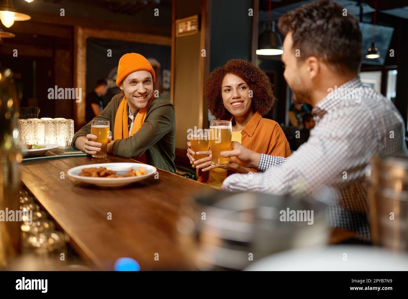 Happy friends drinking beer while rest sitting at bar counter desk ...