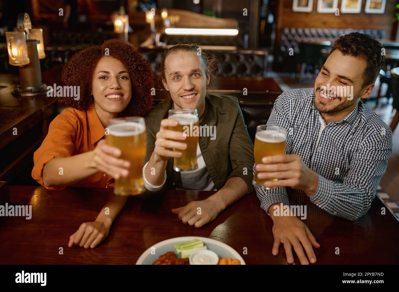 Cheerful friends drinking draft beer at bar table in pub Stock Photo ...