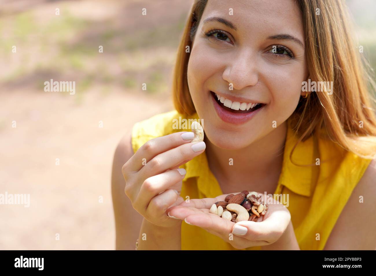 Close-up of smiling girl eating a mix of nuts seed dried fruits looking ...
