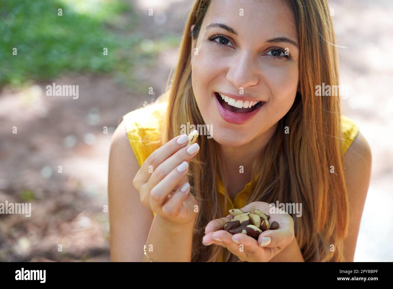 Close-up of healthy woman eating Brazil nuts in the park. Looks at ...