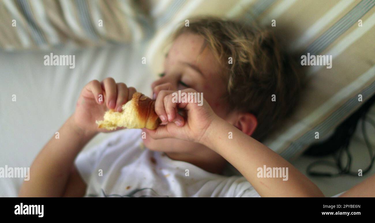 Pensive child thinking while eating croissant. Toddler boy lying on ...