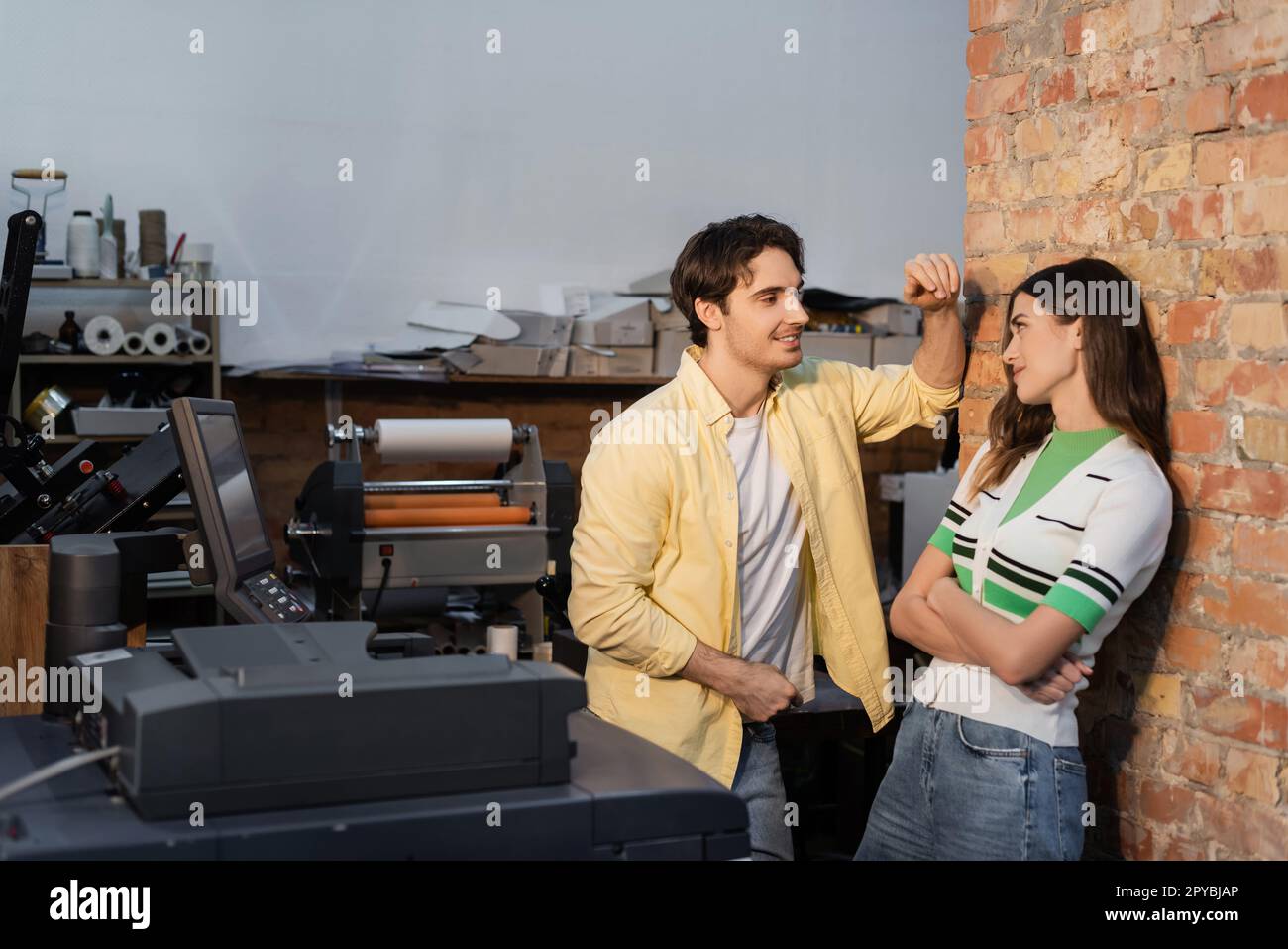 cheerful man flirting with pretty colleague while standing together in ...