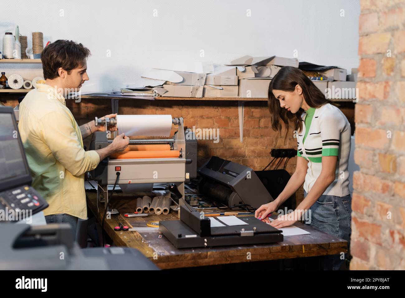 man standing next to flexographic machine and pretty colleague in print ...