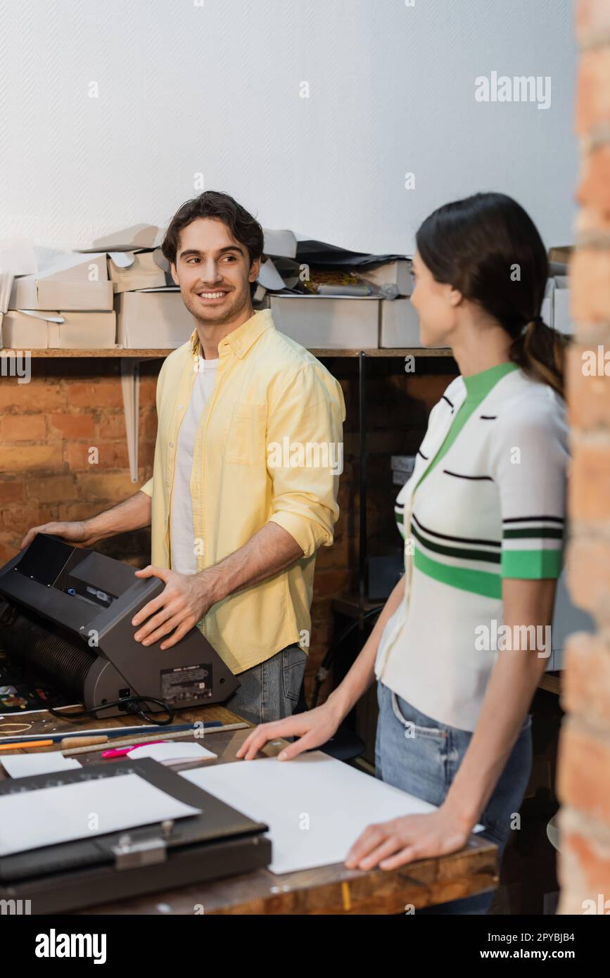 cheerful printing operator looking at colleague while standing near ...