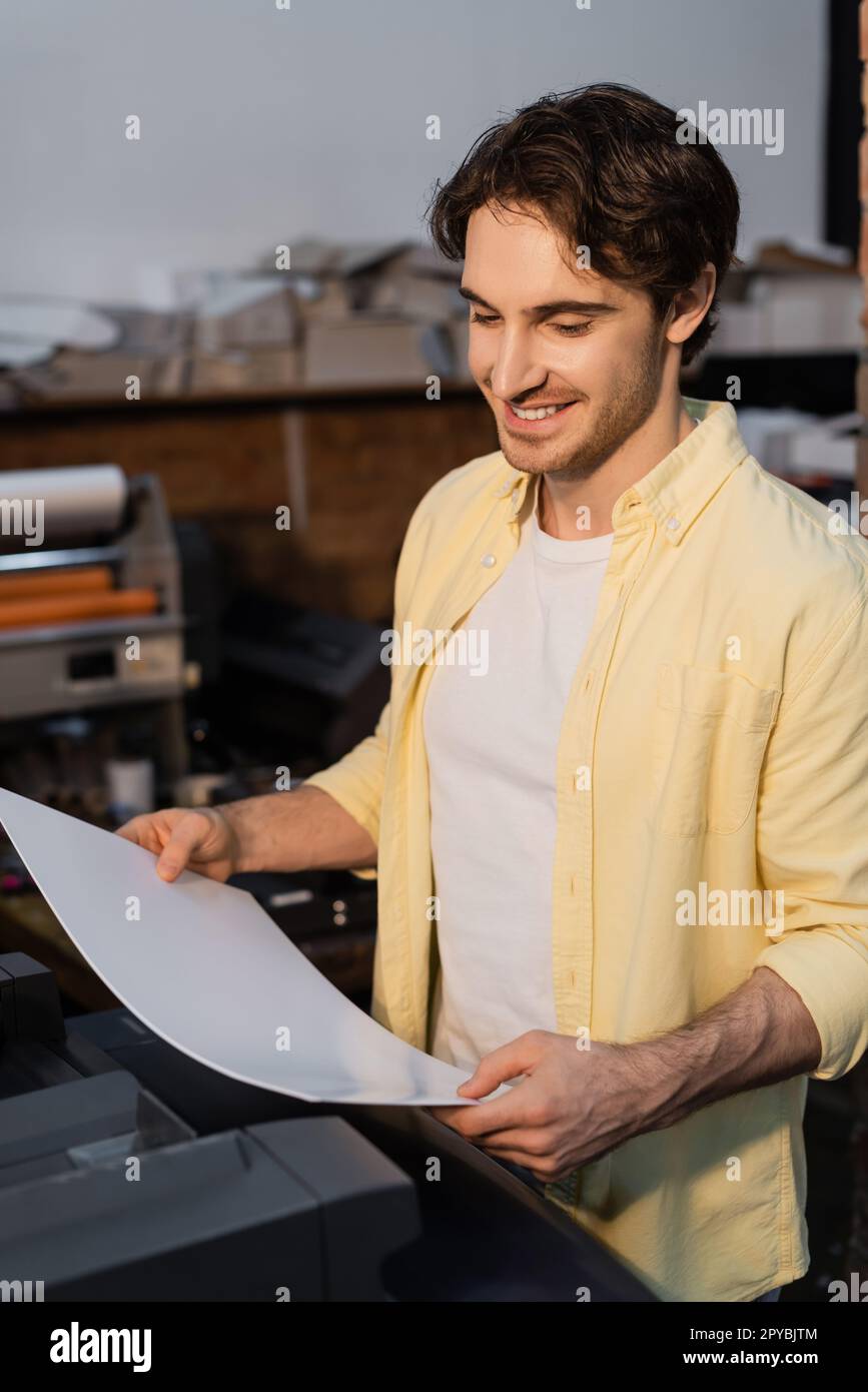 cheerful publisher holding blank paper and smiling in print center ...