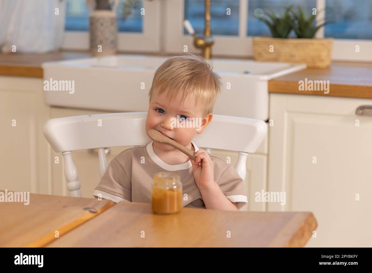 Happy family at home. Baby boy feeding himself in kitchen. Little boy ...