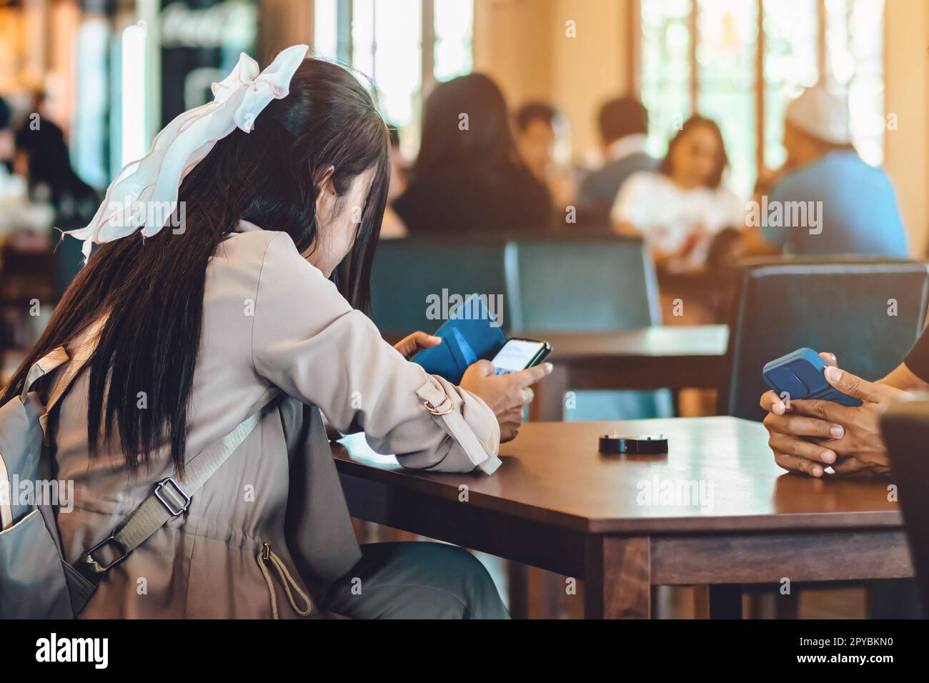 Back view of Woman with white bow hair and backpack using smartphone while waiting food with ...