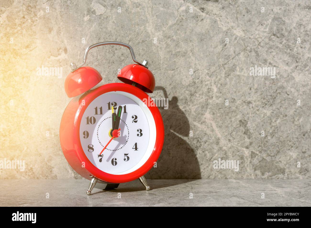 Red alarm clock with a sunlight and shadow on the grey stone background ...