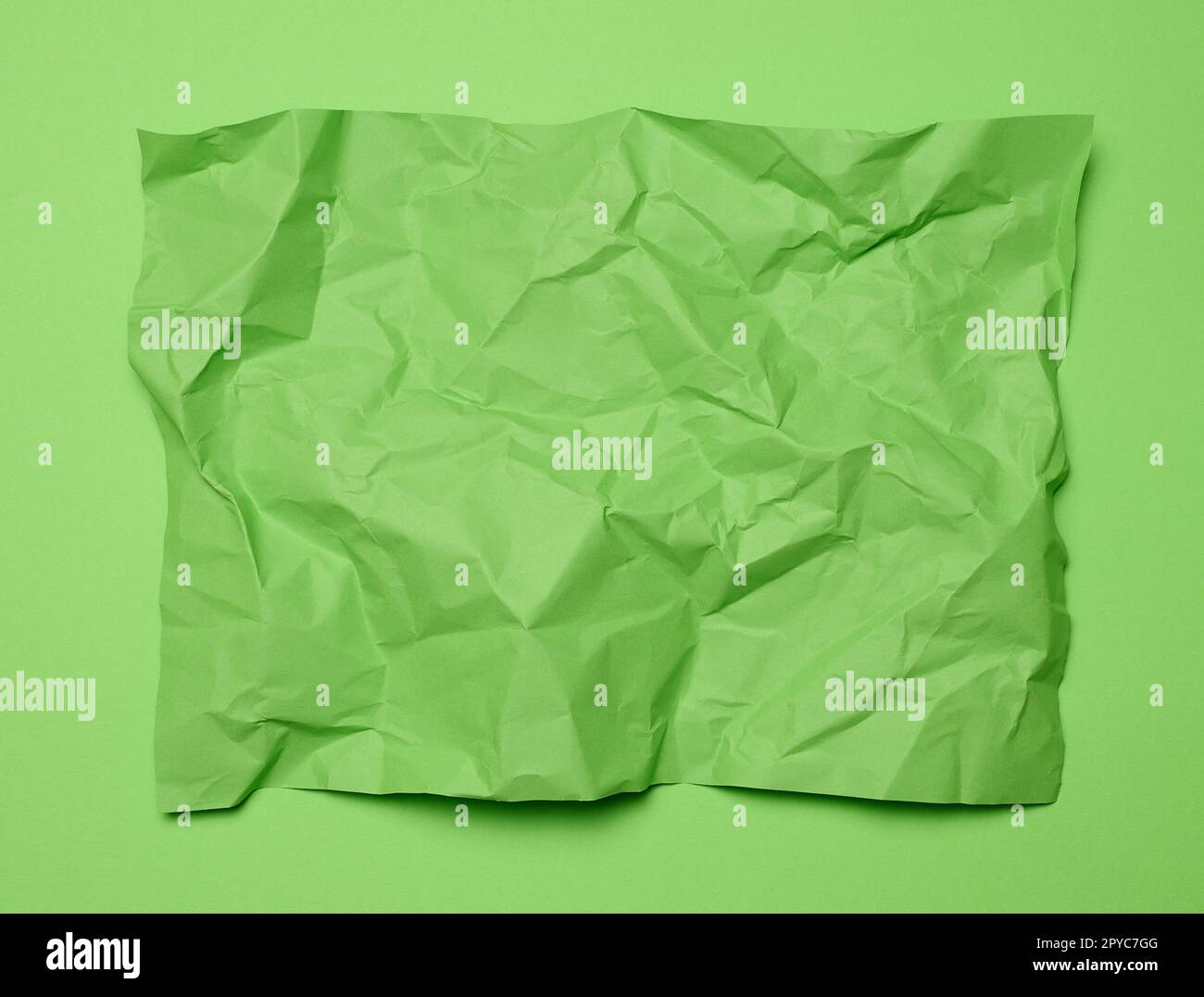 Crumpled rectangular sheet of green paper on a green background, top ...