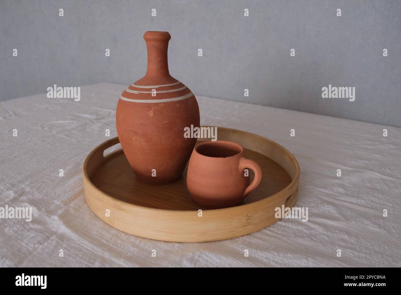 Front view of old unpainted antique ceramic clay pitcher in a tray on a ...