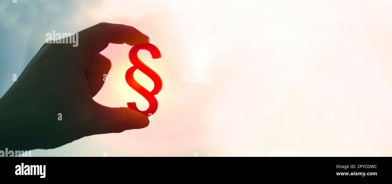 Hand holds paragraph symbol in the sun. Panoramic image with copy space ...