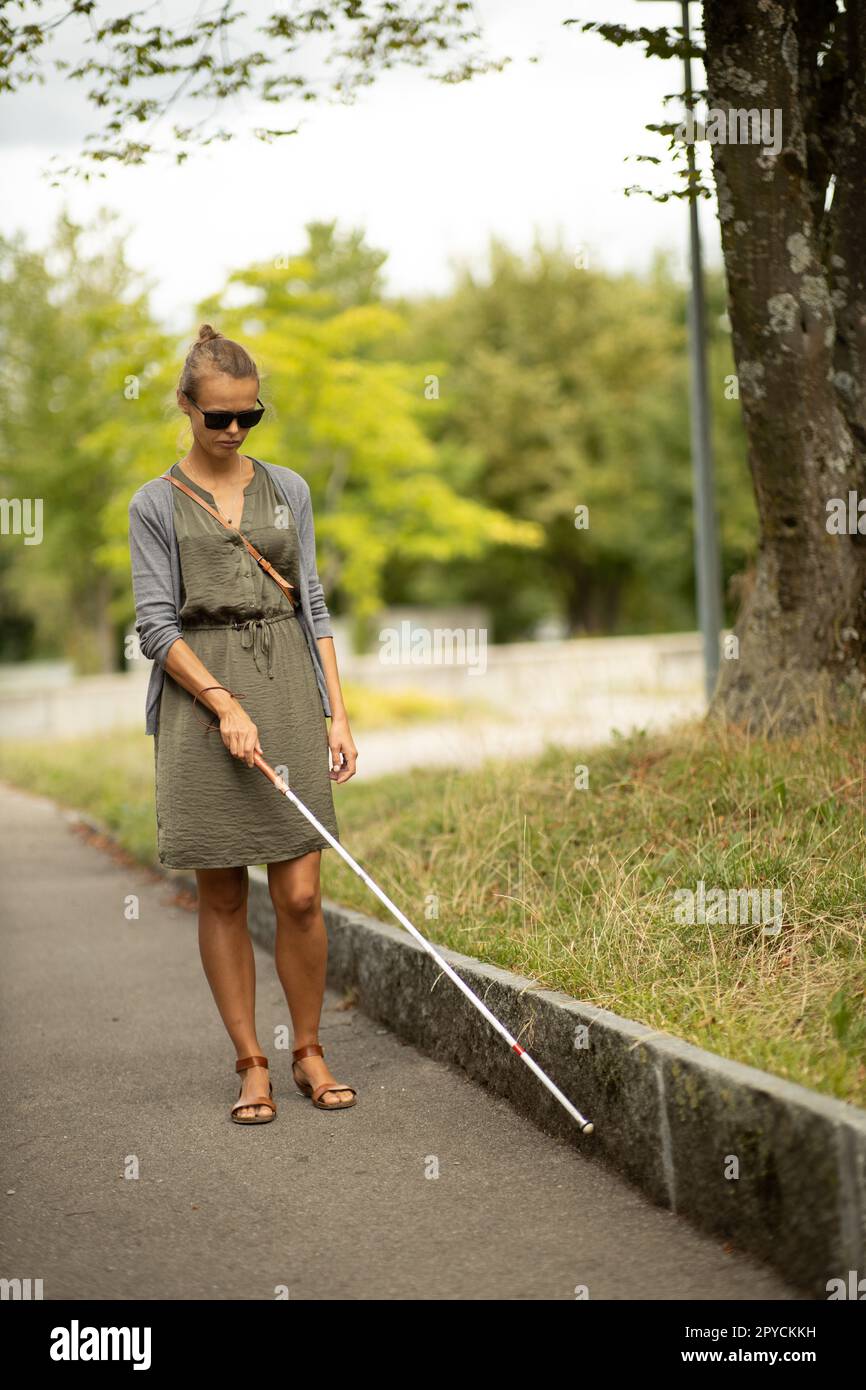 Blind woman walking on city streets, using her white cane to navigate ...