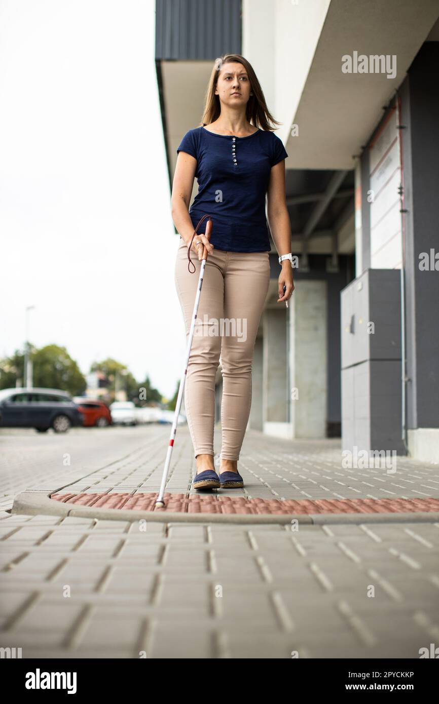 Blind woman walking on city streets, using her white cane to navigate ...