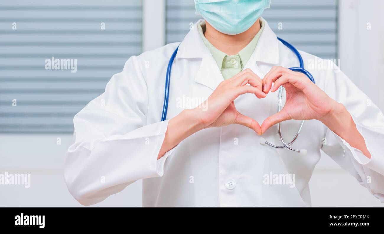 Closeup of doctor woman wearing white coat standing making heart finger ...