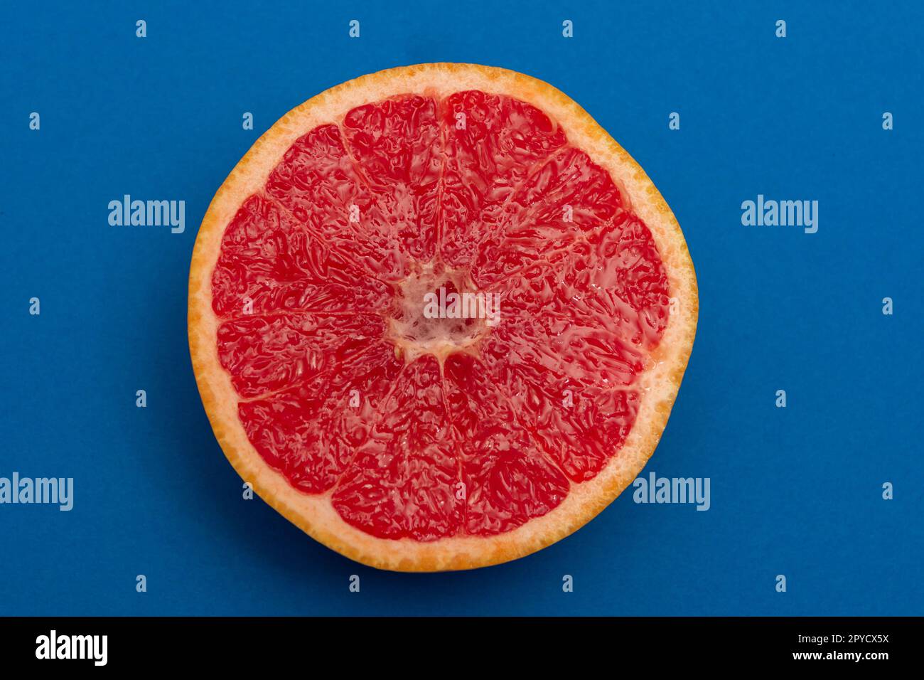 Sliced side of a grapefruit with red pulp isolated on a blue background ...