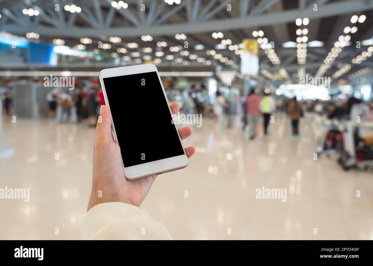 Woman hand using smart phone with blurred airport terminal background ...