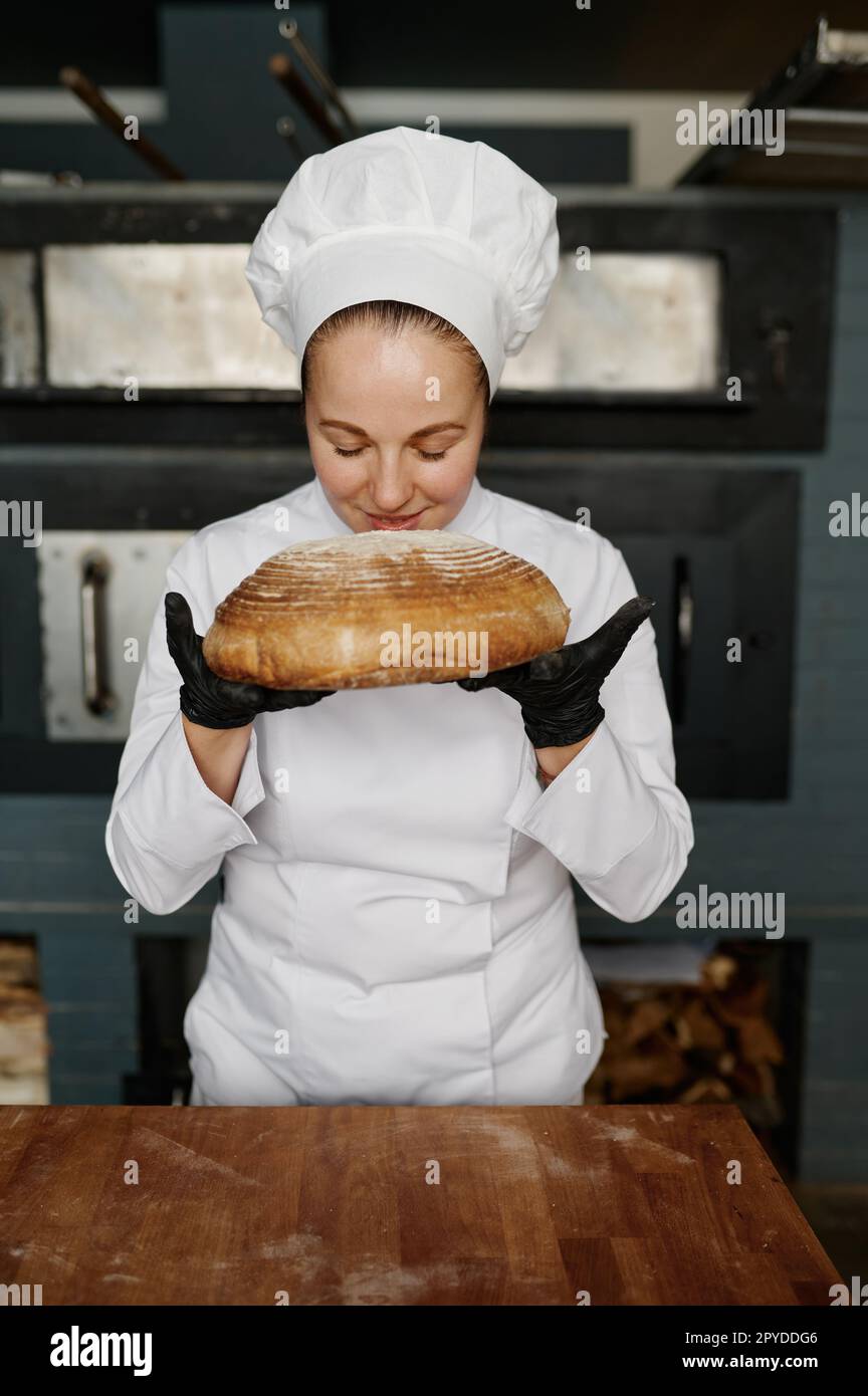 Young female baker smelling fresh bread over modern bakery background ...