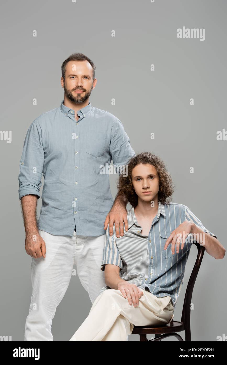 good looking dad standing next to teenage son with curly hair isolated ...