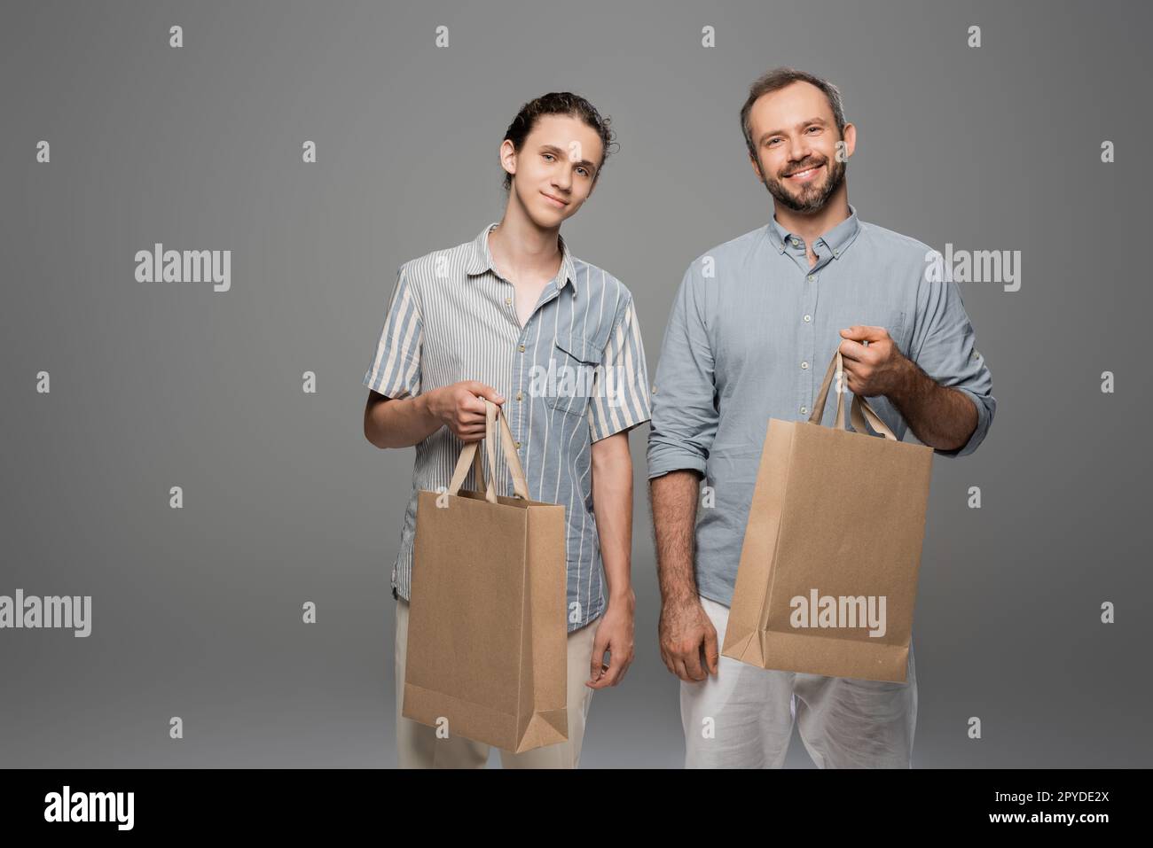 happy teenage boy and dad holding shopping bags isolated on grey,stock ...