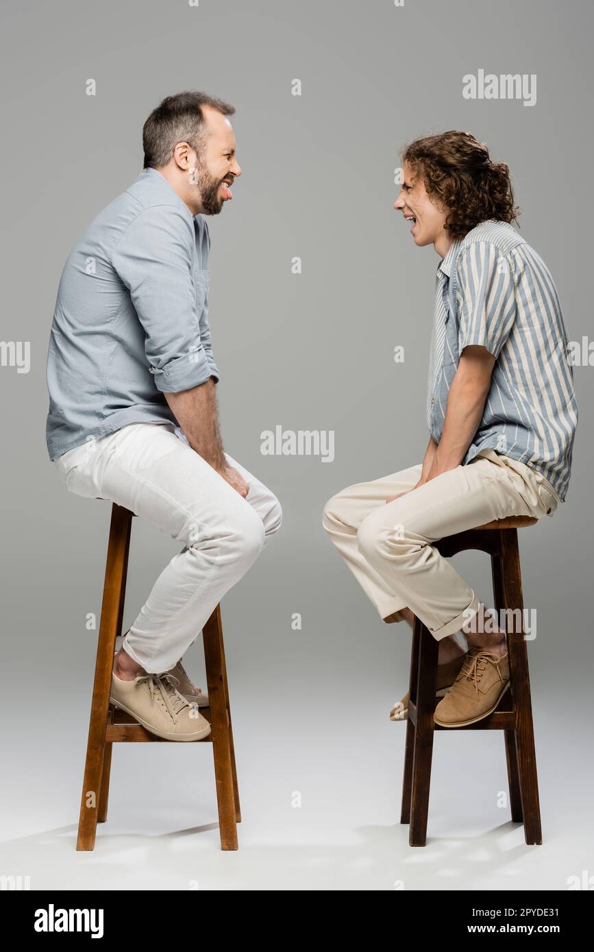 side view of funny dad and teenage son grimacing at each other while ...