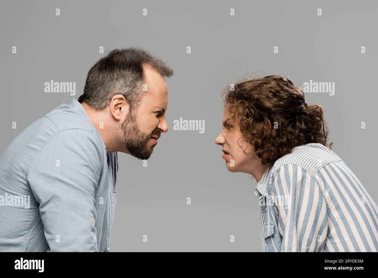 side view of angry dad and irritated teenage son looking at each other ...