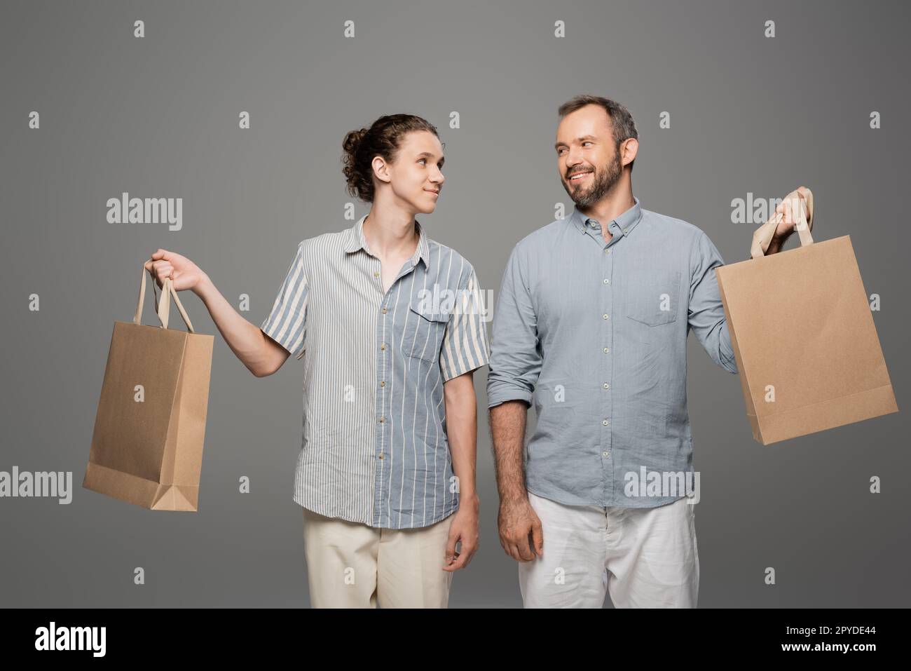 happy teenage boy and cheerful dad holding shopping bags isolated on ...