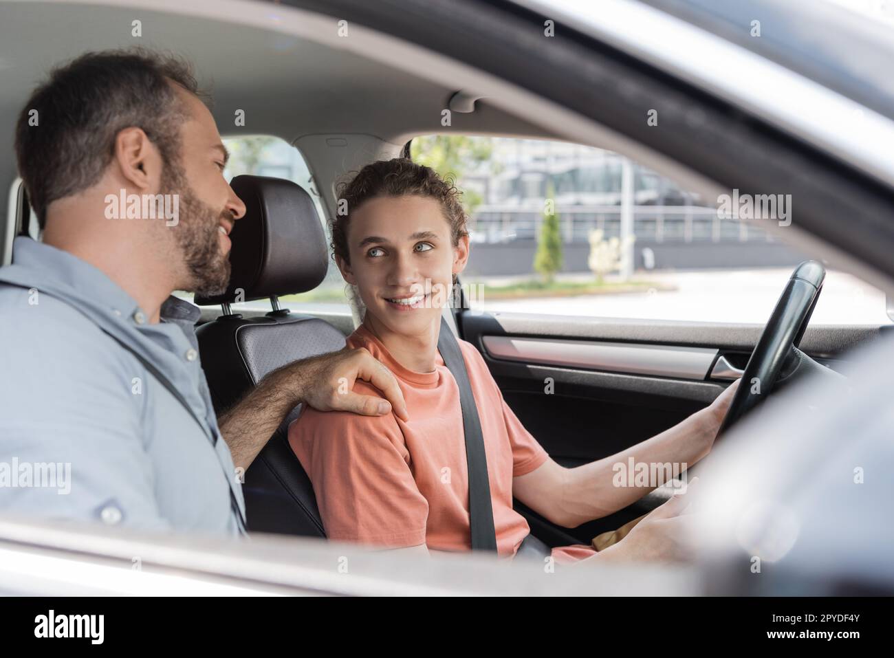 cheerful father putting hand on shoulder of teenage son while teaching ...