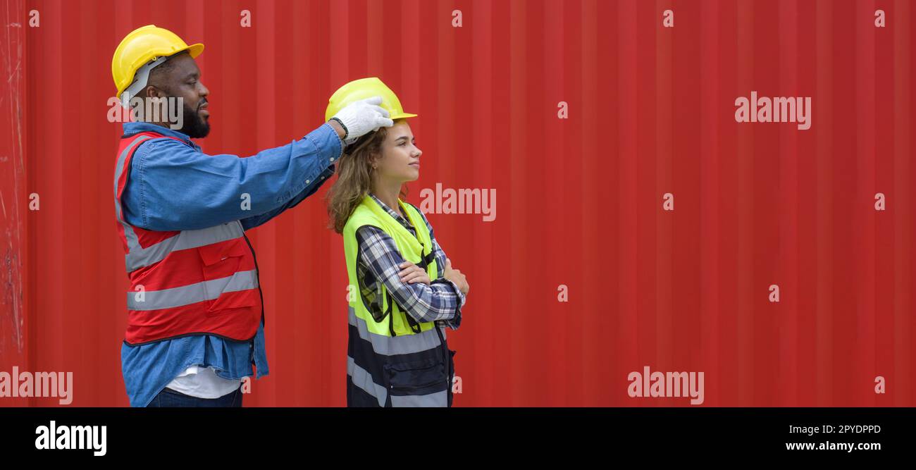 A foreman with mustache and beard helps a female apprentice wear a ...