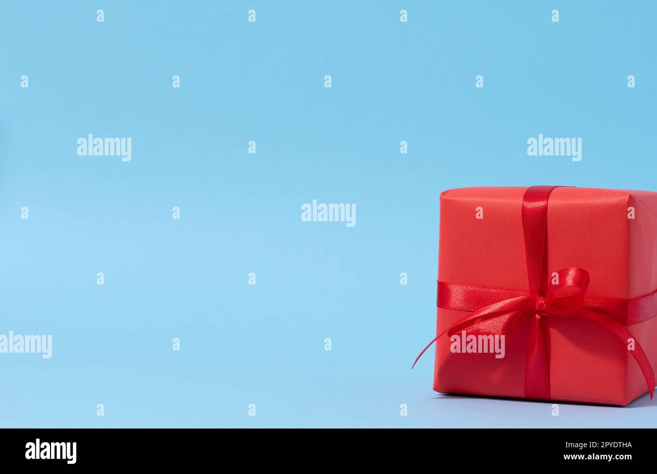A square red gift box with a red ribbon on a blue background ...