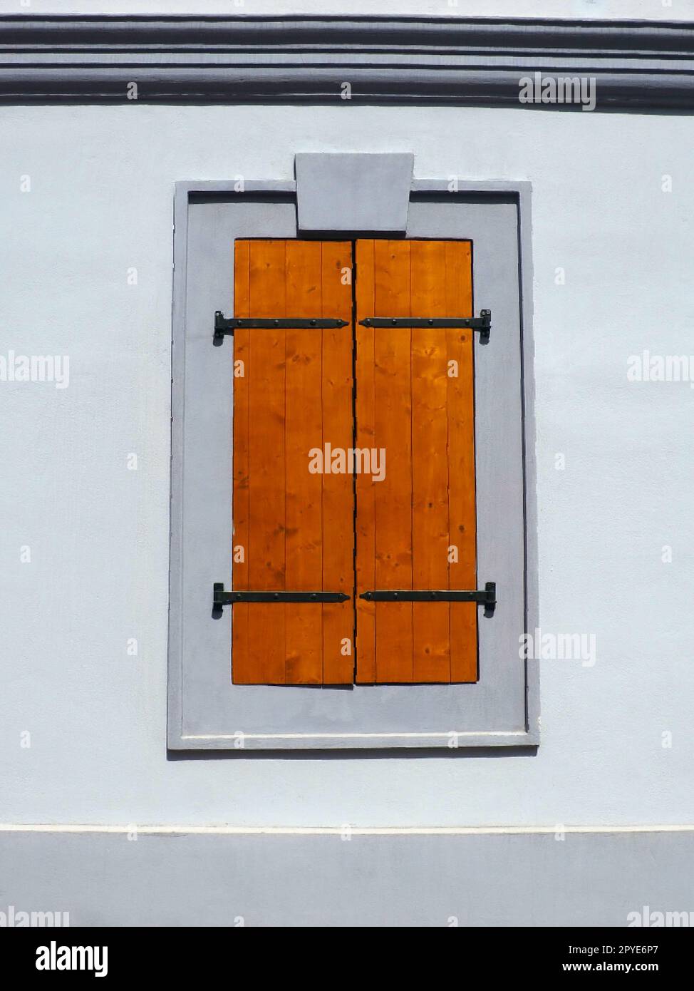 Window with old wooden shutters. Metal curly braces. White wall ...