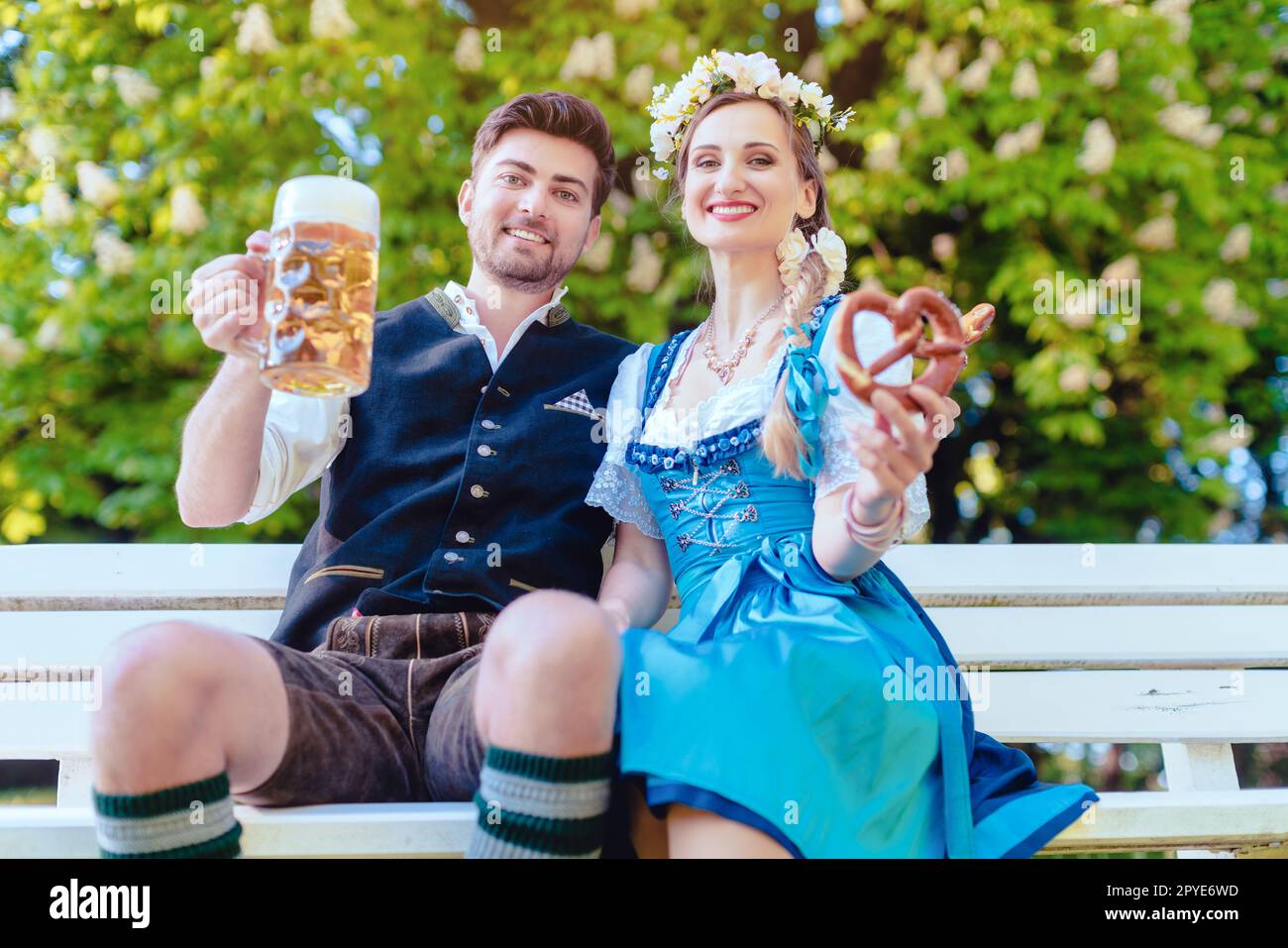 Couple in Bavaria sitting on bench toasting with beer Stock Photo - Alamy
