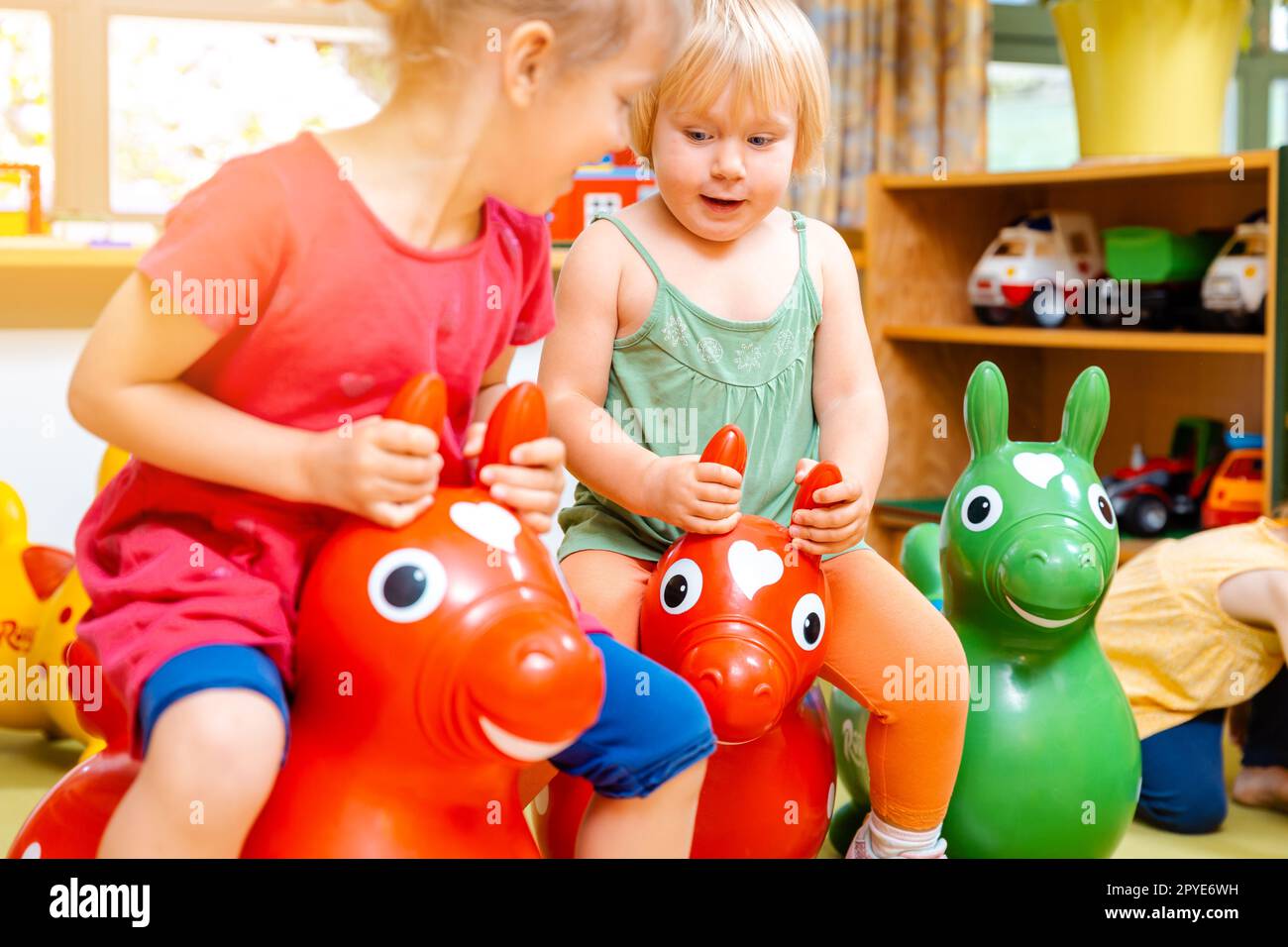 Little girls riding on play horses in kindergarten Stock Photo - Alamy