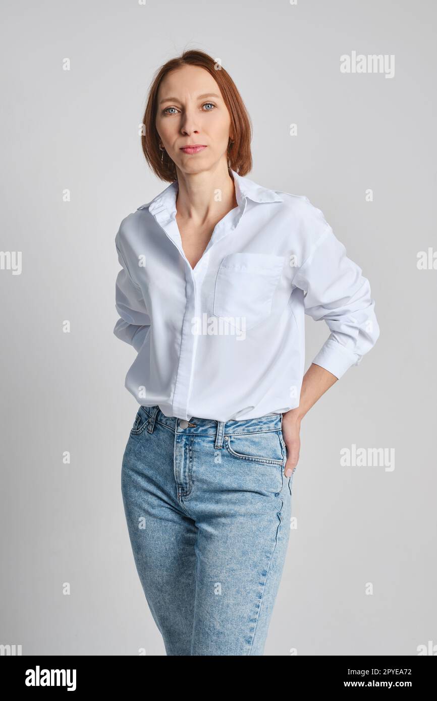 Portrait of redhead woman standing against grey background with arms in ...