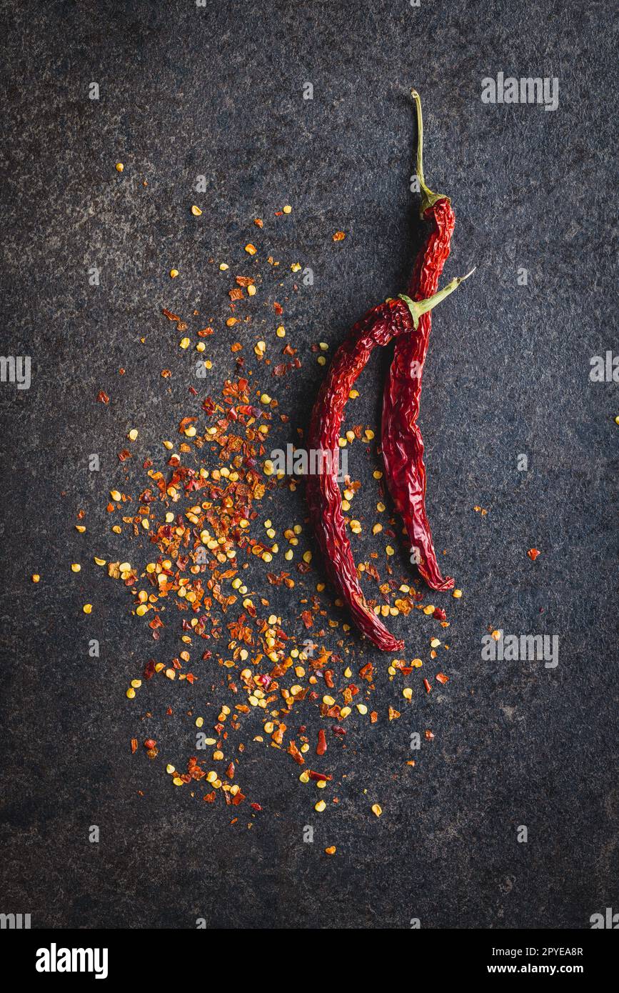 Dry chili pepper flakes. Crushed red peppers on black table. Top view ...