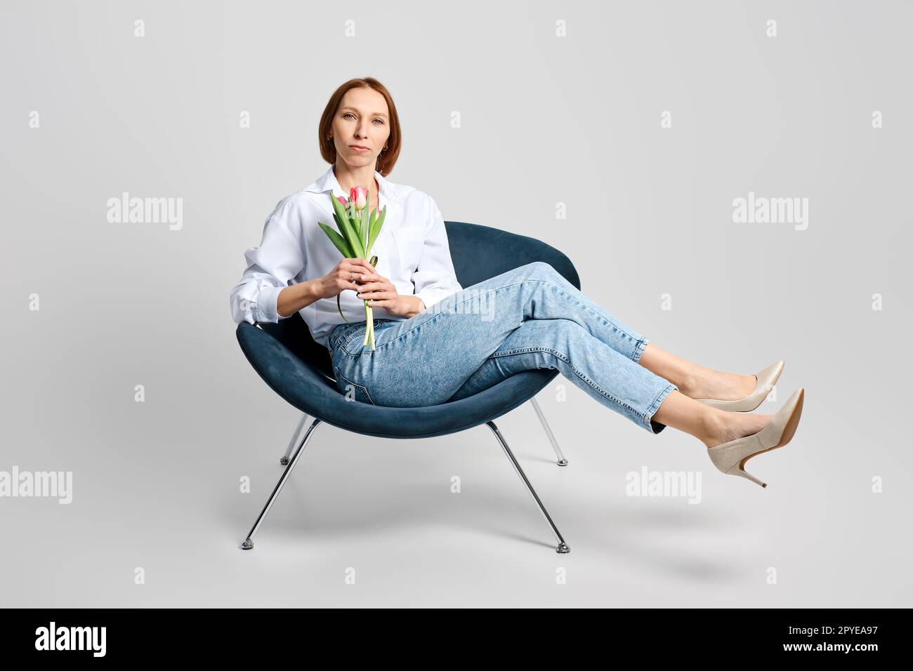 Portrait of cheerful meddle aged woman in armchair with tulips in hand ...