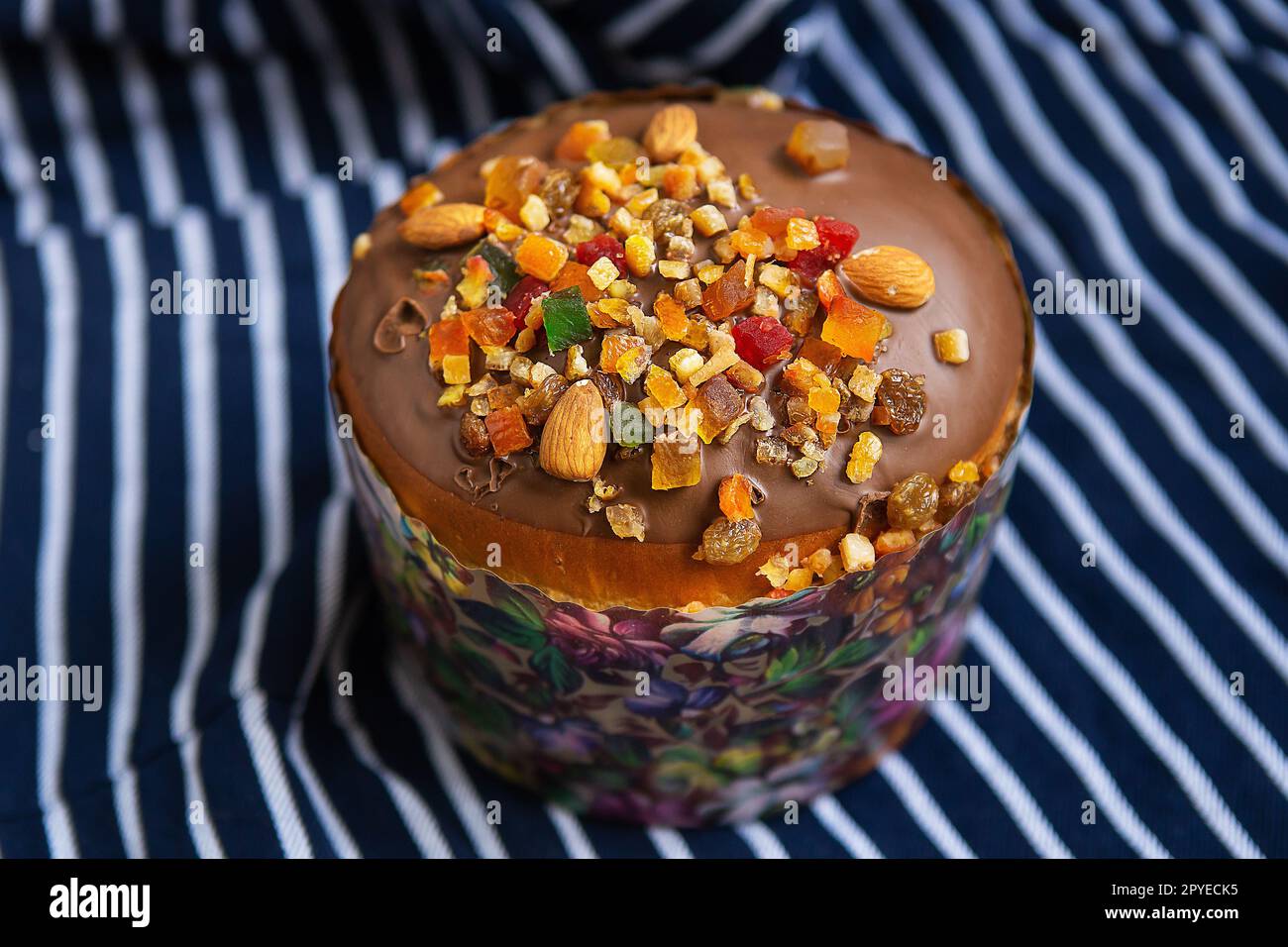 An Easter cake decorated with candied fruits stands on a striped blue ...