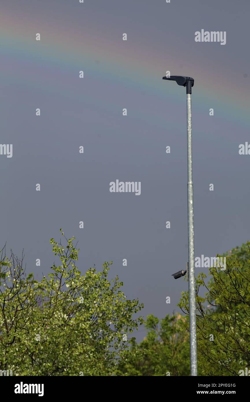 Rainbow on a grey sky after a storm with tree tops and street lamp in ...