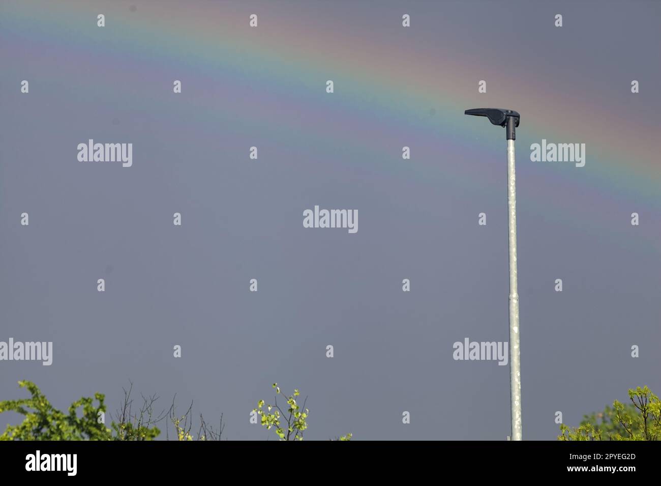 Rainbow on a grey sky after a storm with tree tops and street lamp in ...