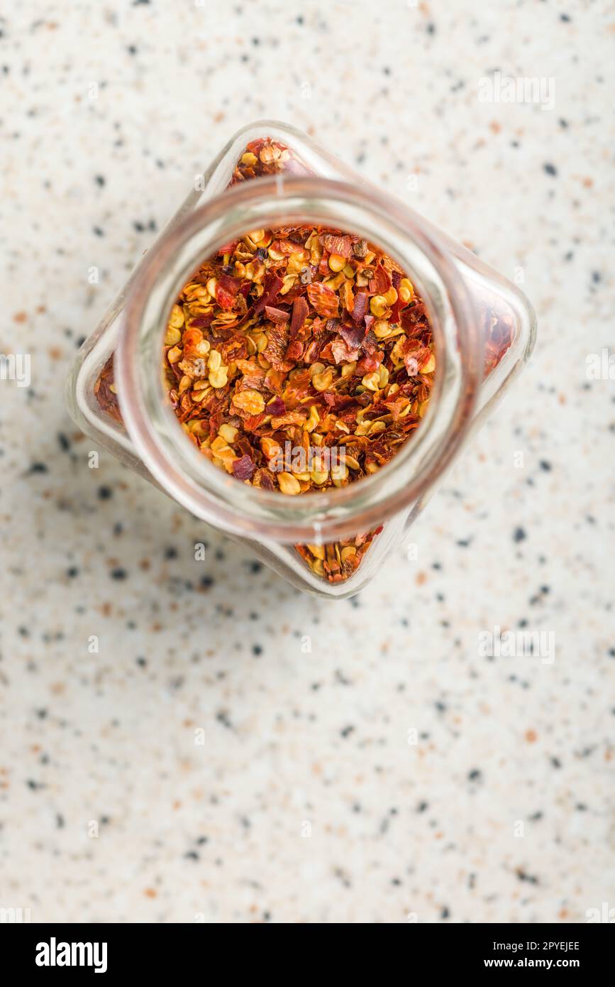 Dry chili pepper flakes. Crushed red peppers in jar on white table. Top ...