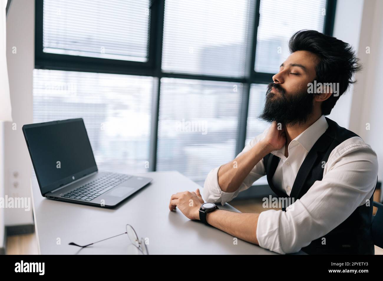 Side view of young tired Indian employee IT businessman hold put hand ...